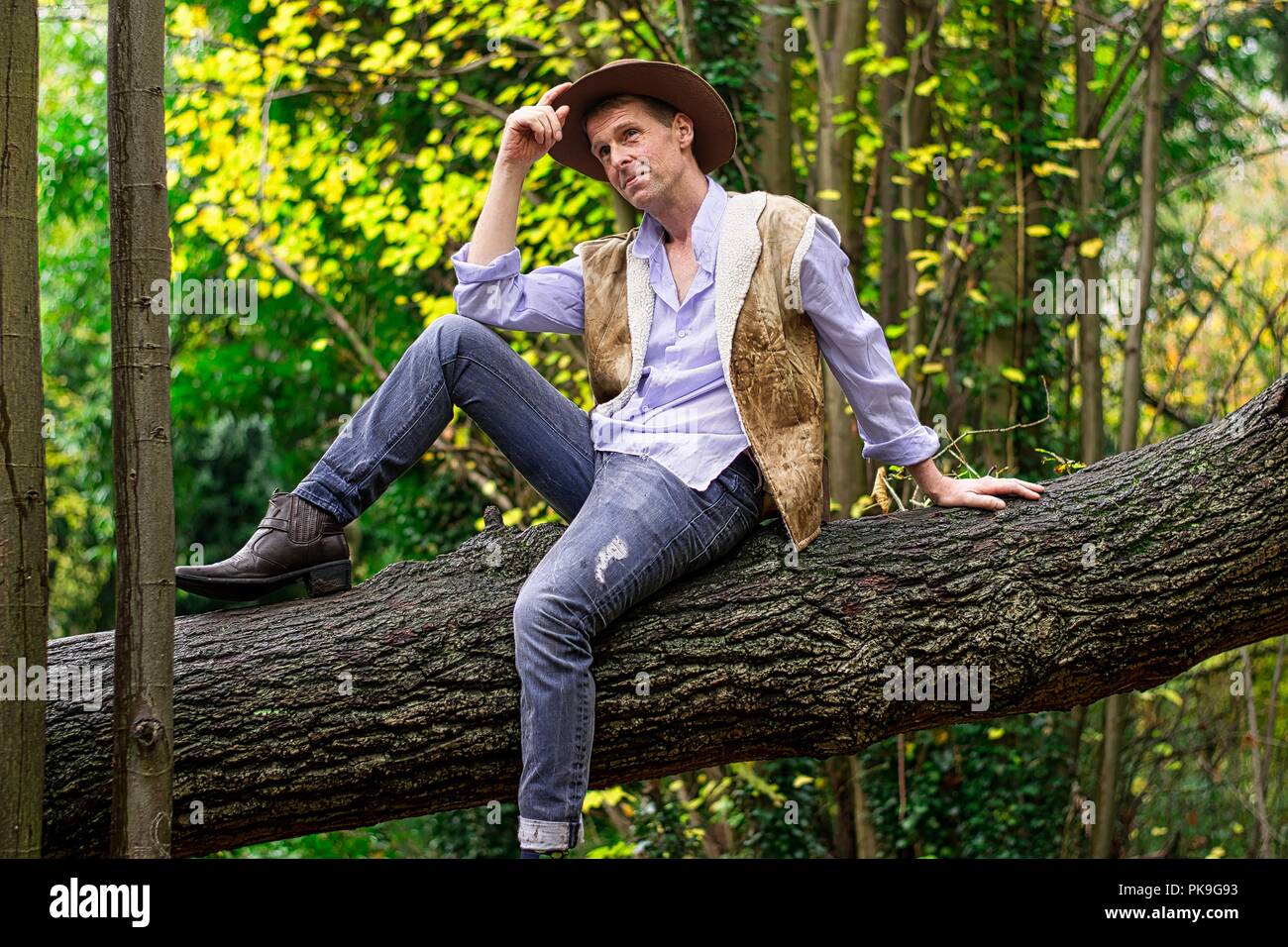 A man dressed like a cowboy sites on a fallen tree branch Stock Photo ...