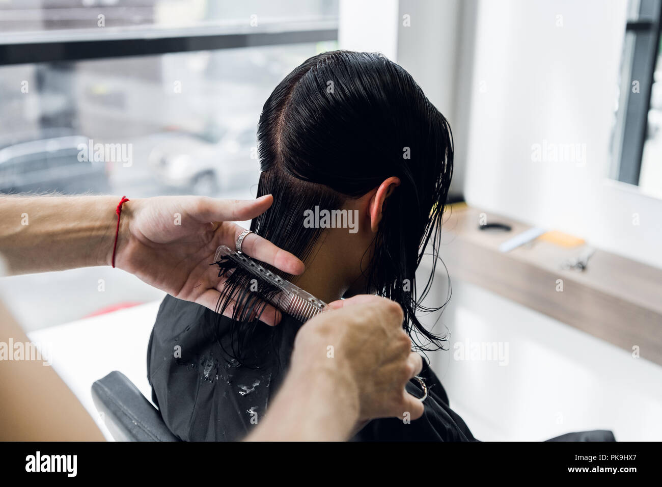 Man's hands cut and comb female dark brown hair in a beauty salon with ...