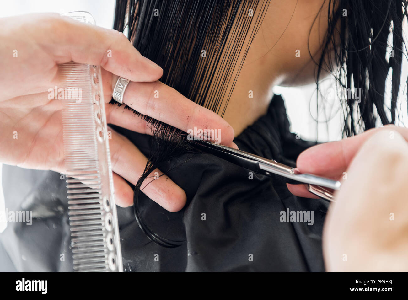 Man's hands cut and comb female dark brown hair in a beauty salon with ...