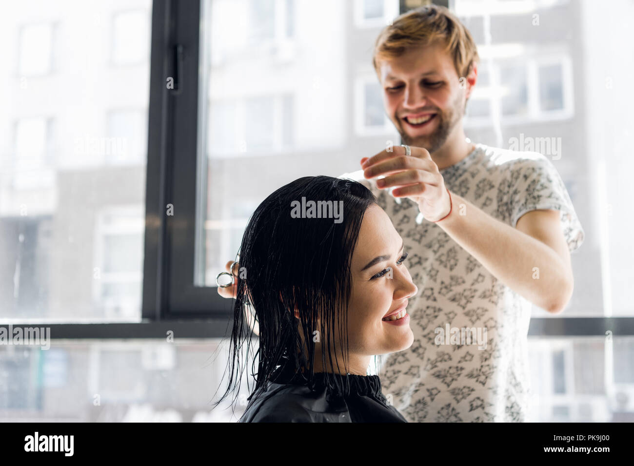 Laughing girl and hairdresser talking and smiling while making a new ...