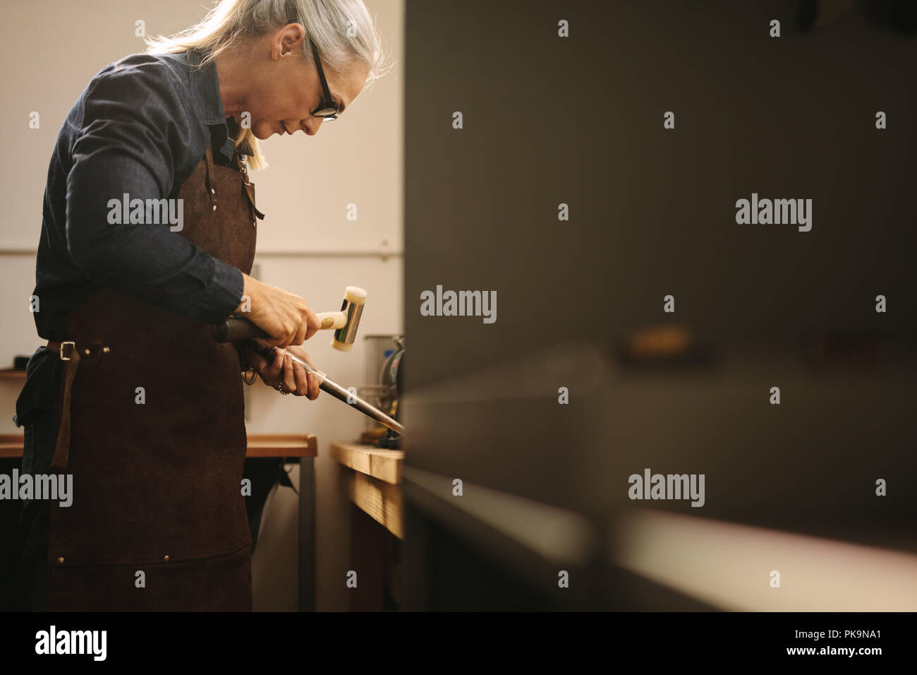 Senior woman making jewelry using traditional tools in her workshop ...