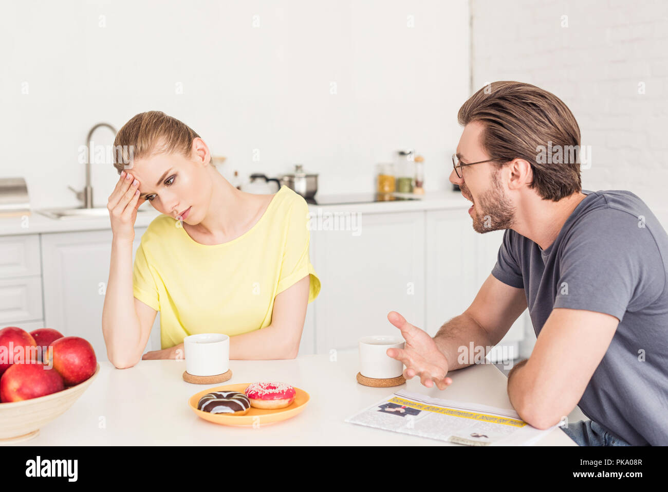 angry man screaming at upset girlfriend while she sitting at table with ...