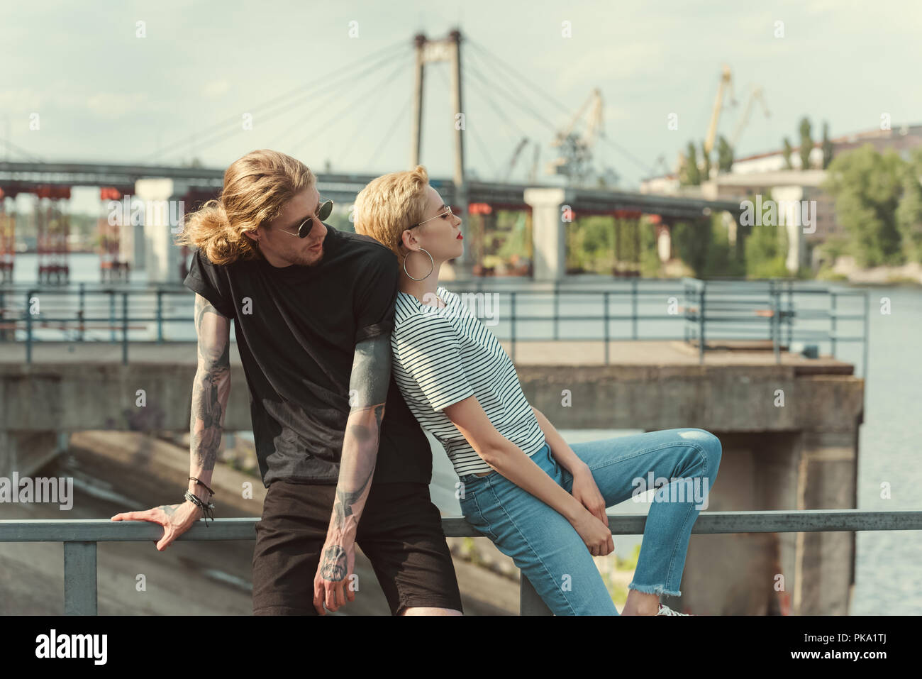 boyfriend with tattoos and stylish girlfriend touching with backs and ...