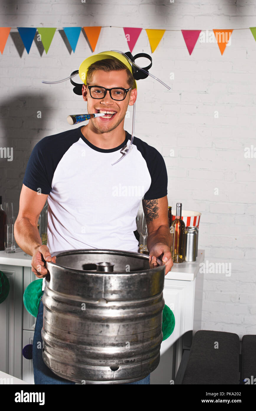 happy young man in beer hat holding keg of beer and smiling at camera ...