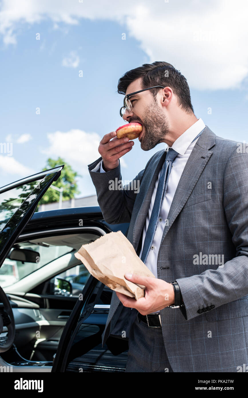 side view of businessman eating take away doughnut while standing at ...