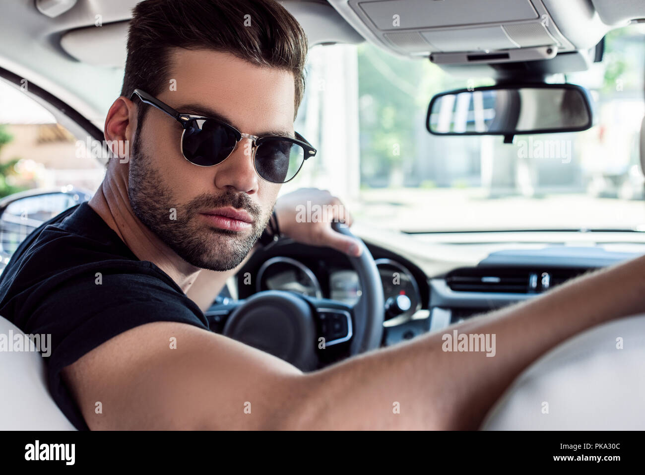 portrait of serious stylish man in sunglasses looking back while ...