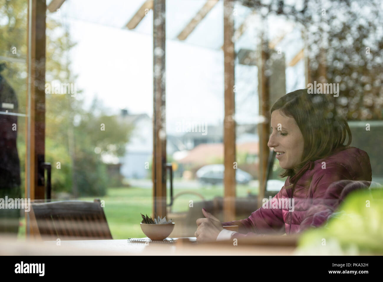 View through a glass window of a young woman sitting in a cafe alone ...