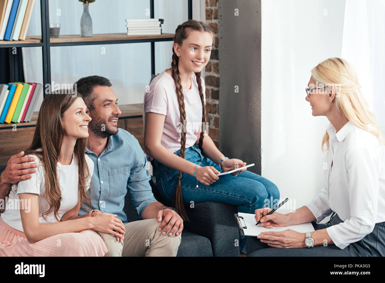 female counselor writing in clipboard on therapy session of family with ...