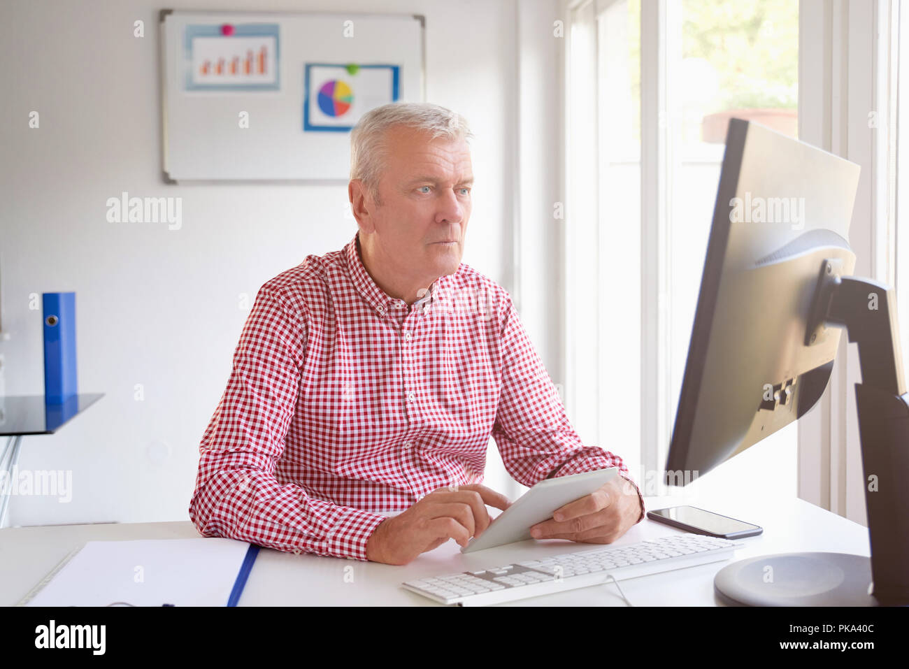 Senior sales manager using digital tablet while sitting at office desk ...