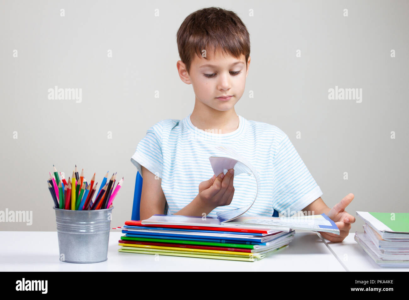 Boy sitting at desk with pile of school books and notebooks and doing ...