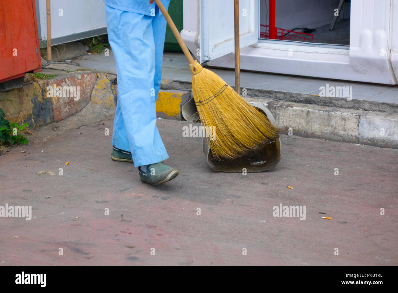 City street male or female sweeper cleaning pavement with old broom ...