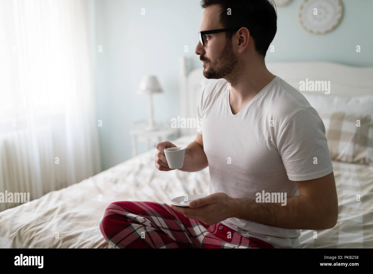 Handsome man drinking morning coffee sitting on bed Stock Photo - Alamy
