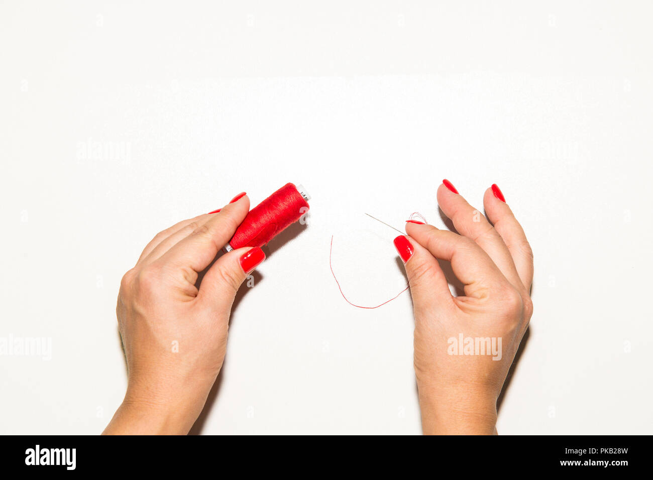 Female hand seamstress, needlewoman holding in hands red thread and ...