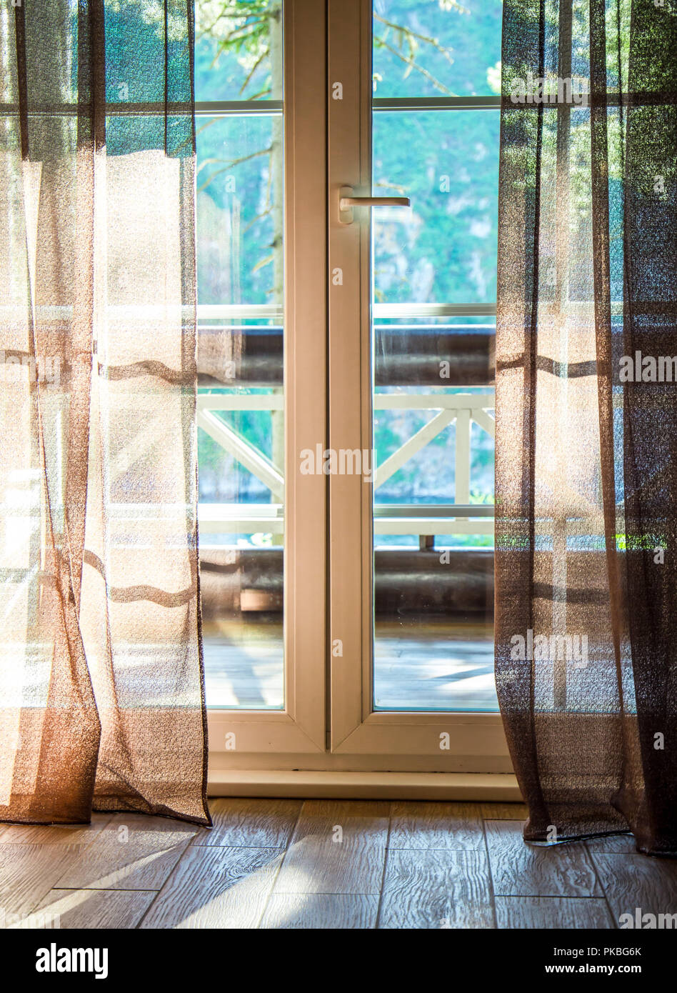 French doors open onto a balcony with a view of leafy green trees ...