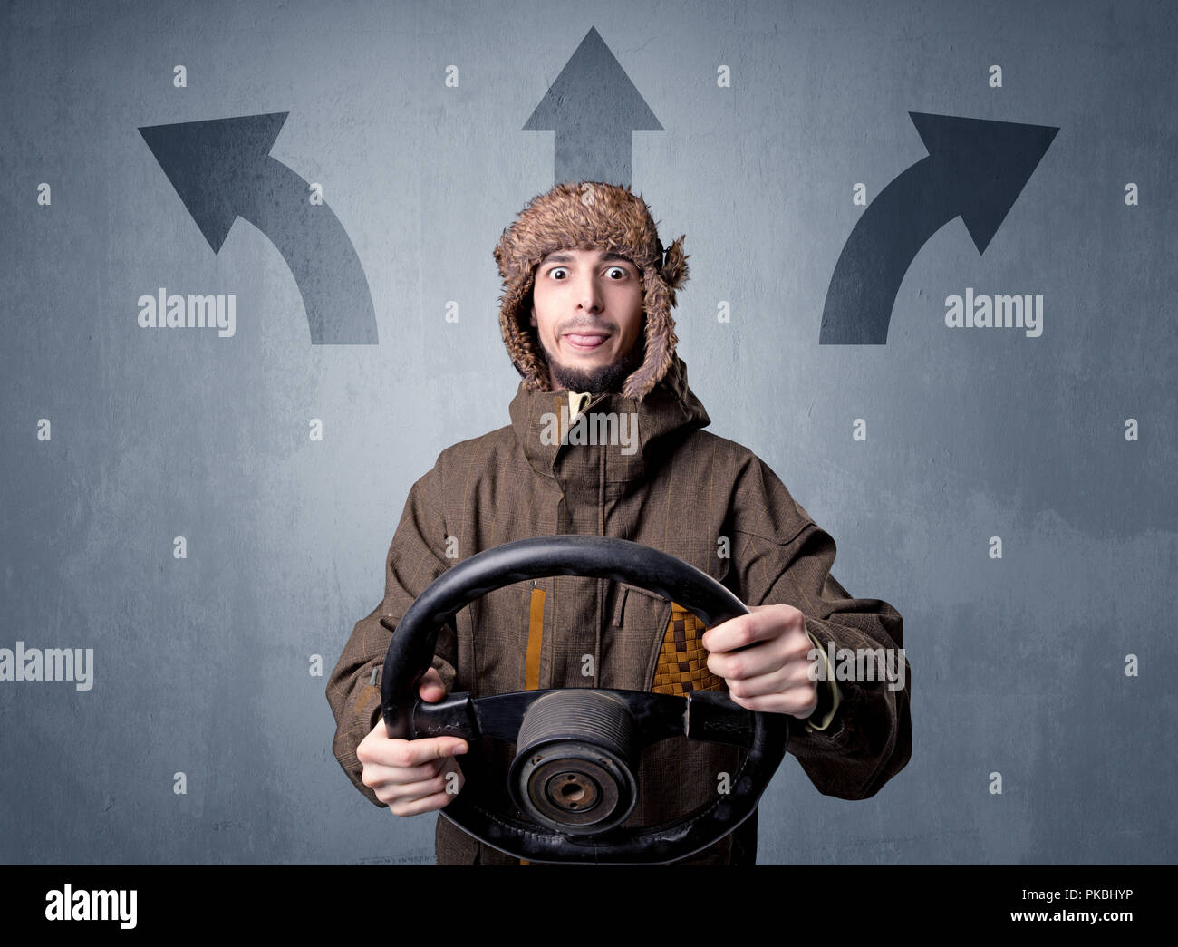 Young man holding black steering wheel with three arrows above his head ...