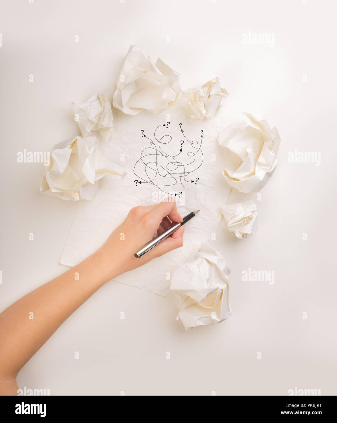 Female hand next to a few crumpled paper balls drawing random scribbles ...