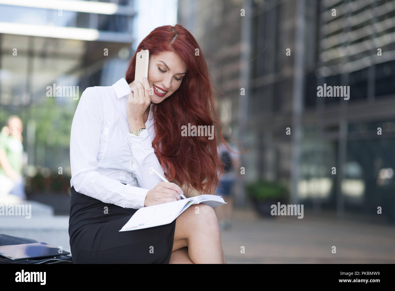 Smiling businesswoman talking on the cellphone while writing on her ...