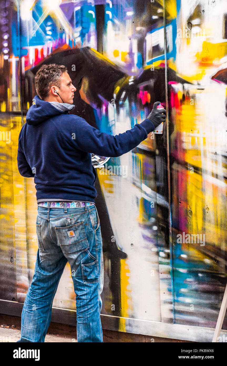 A graffiti artist creating a colourful rainy night time street scene ...