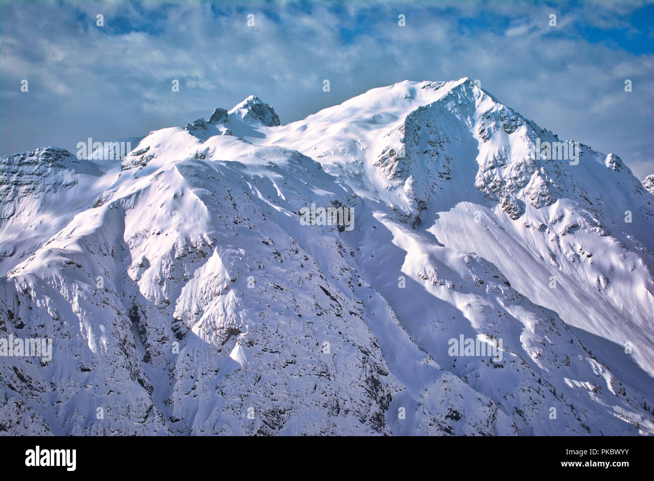 Scenery of alpine mountain peaks, covered in snow, with a cloudy sky ...