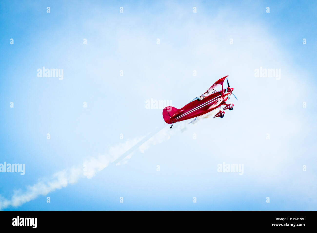 Red airplane with propellers and white smoke on the tail flying in the ...