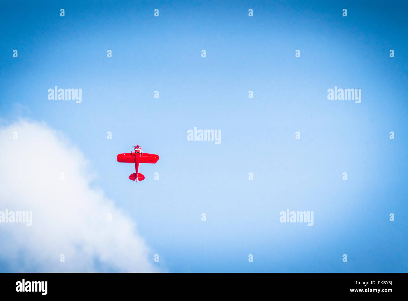 Red propeller plane flying upwards on a blue heaven with white clouds ...