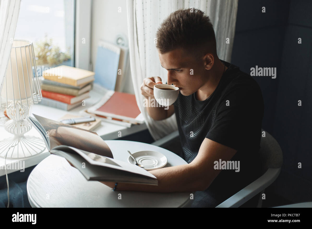 Handsome young guy with coffee reading a book at the table Stock Photo ...