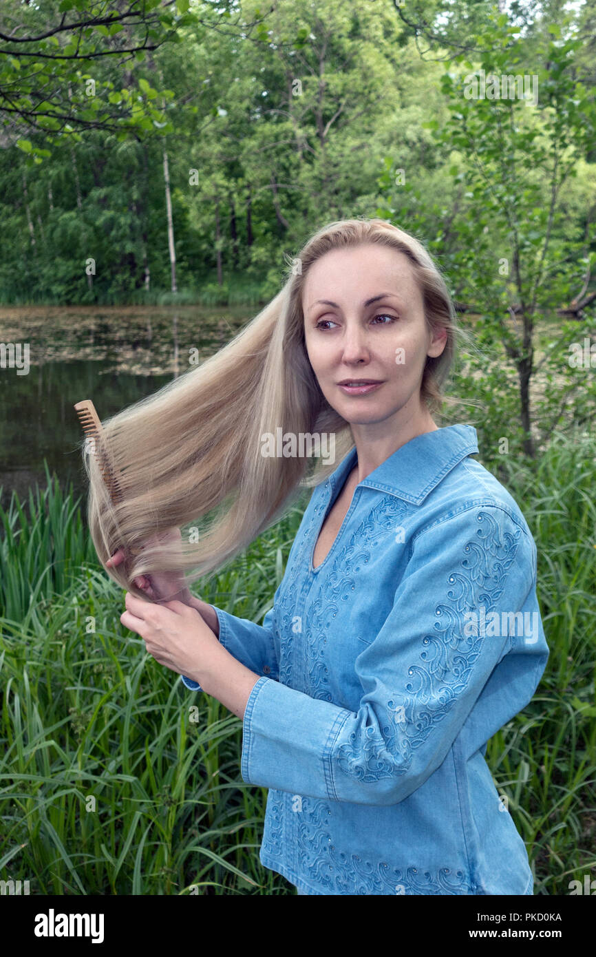 Beautiful woman combs long hair in the summer day on the river bank ...