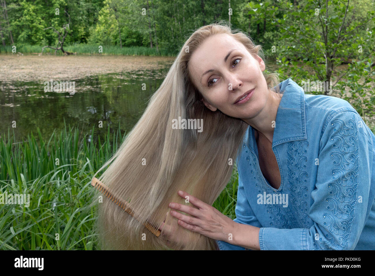 Beautiful woman combs long hair in the summer day on the river bank ...