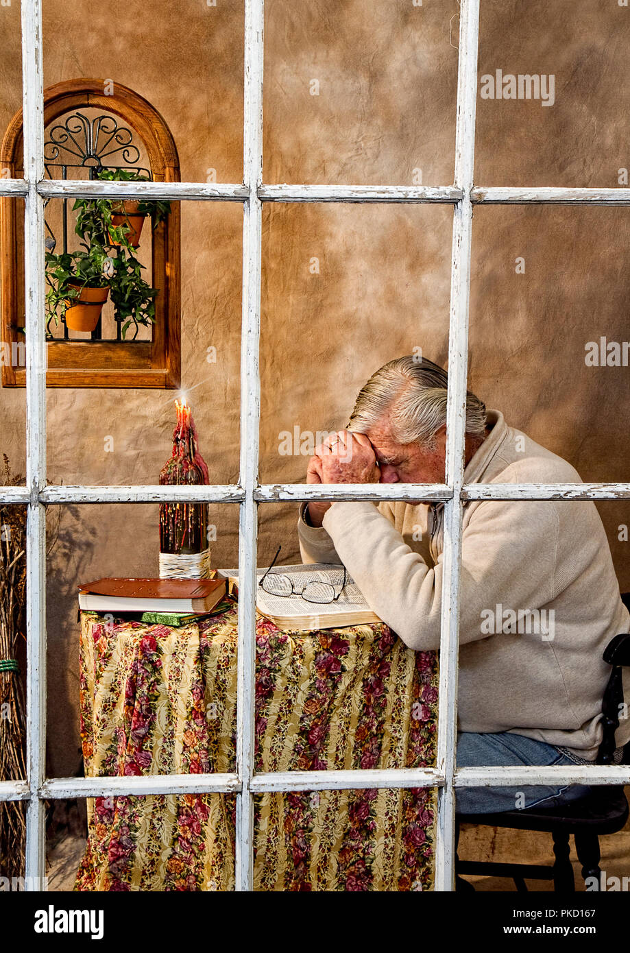 View through old worn window of a male senior citizen praying and/or ...