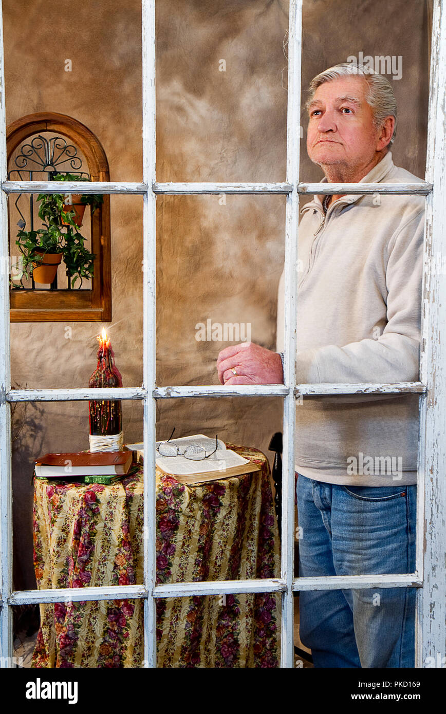 View through old worn window of a male senior citizen praying and/or ...