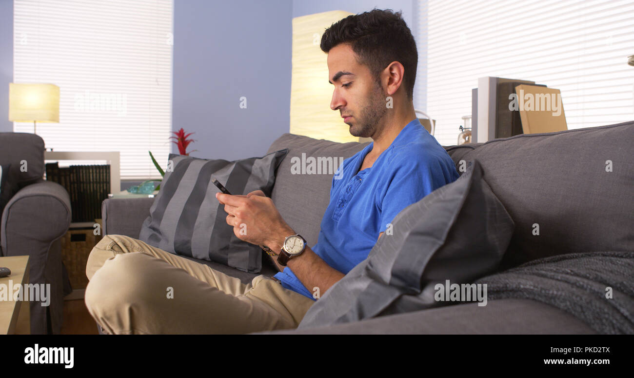 Mexican man smiling and texting on couch Stock Photo - Alamy