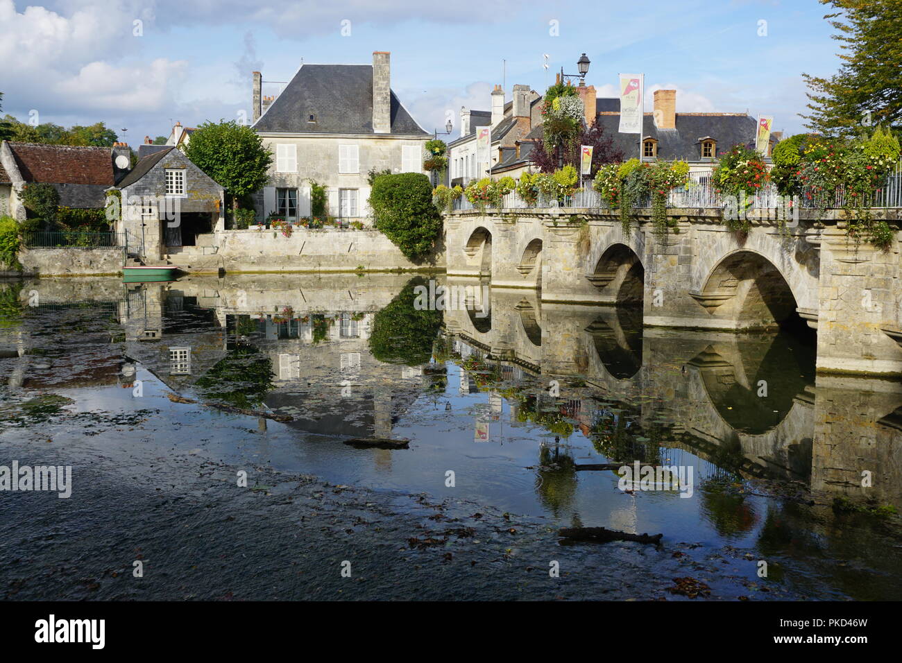Mirror reflection of an old stone bridge and small town in the river on ...