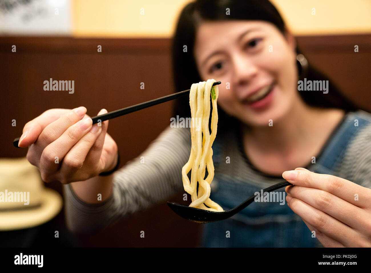 the closeup view of a young female eating undon with chopsticks and ...