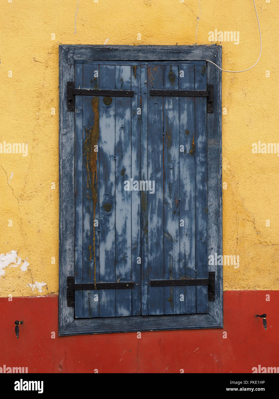 Rustic faded blue wooden window shutters in yellow and red wall of ...