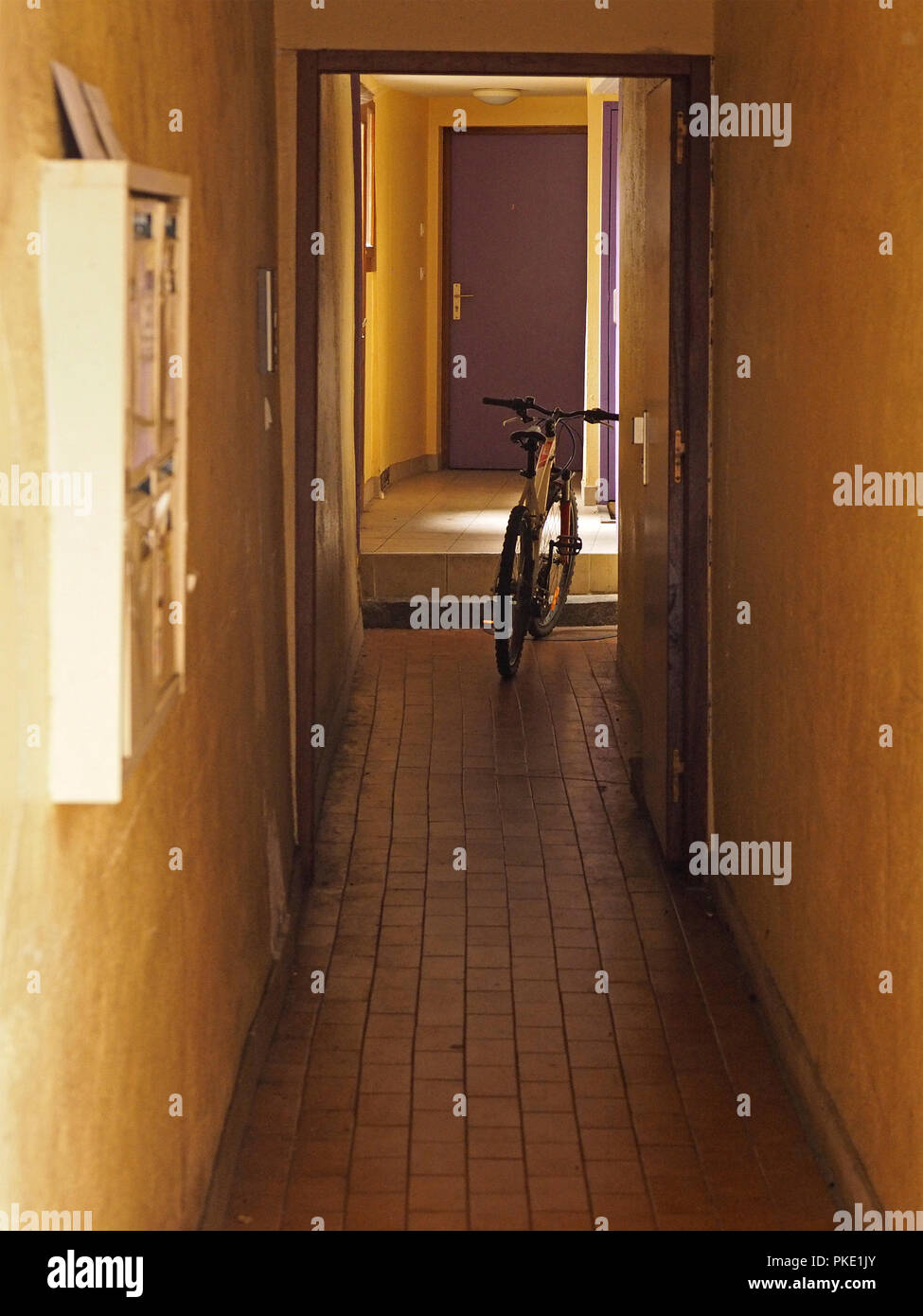 View down tiled passageway with open doorways and bicycle in building ...
