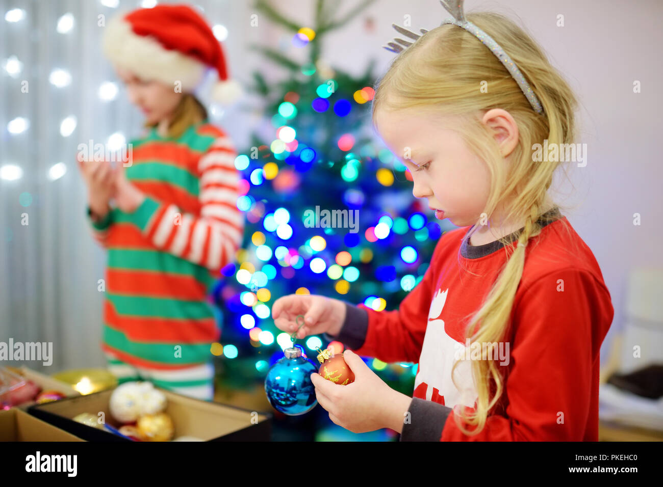 Two adorable sisters decorating a Christmas tree with colorful glass ...