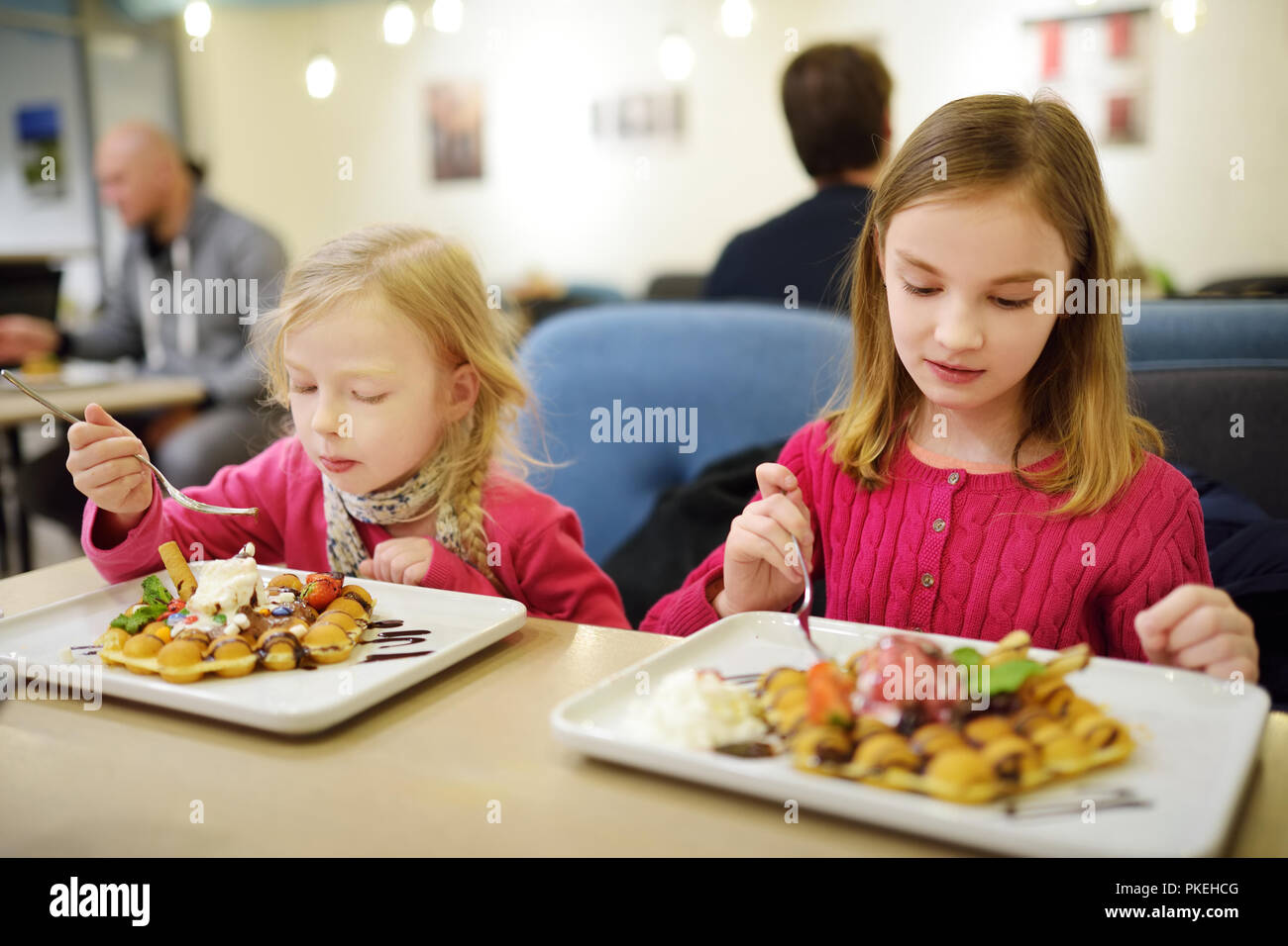 Adorable little sisters eating bubble waffle with fruits, chocolate and ...