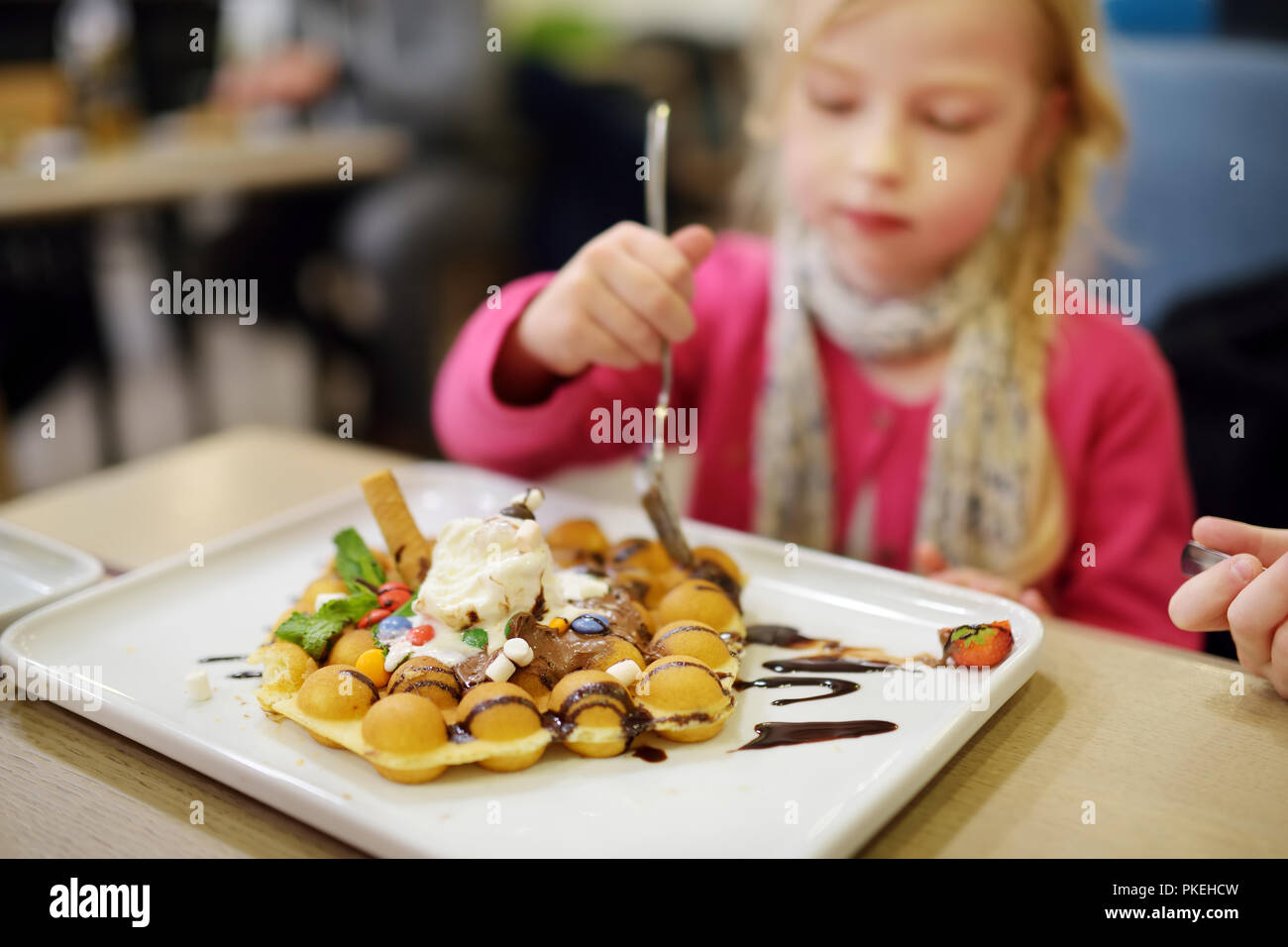 Adorable little girl eating bubble waffle with fruits, chocolate and ...