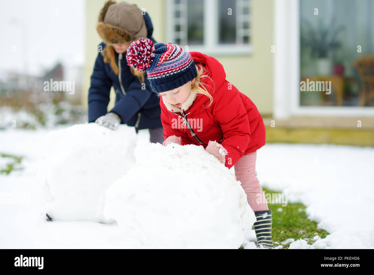 Adorable little girls building a snowman in the backyard. Cute children ...