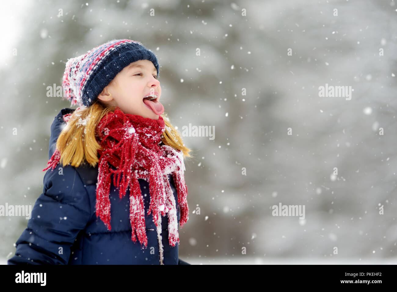 Adorable little girl catching snowflakes with her tongue in beautiful ...