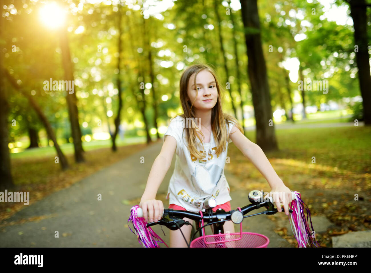 Cute little girl riding a bike in a city park on sunny summer day ...