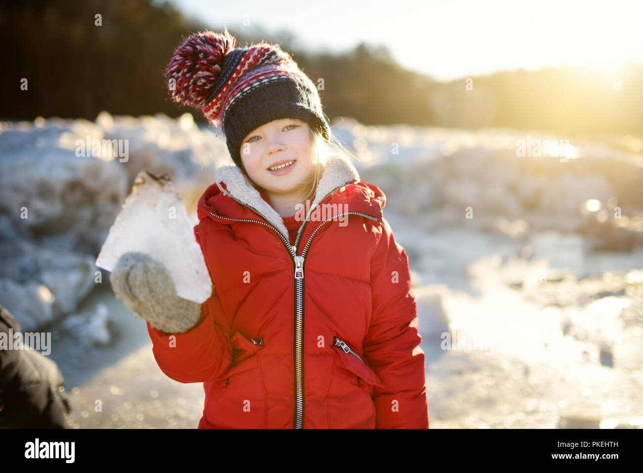 Happy little girl playing with ice blocks by frozen river during an ice ...