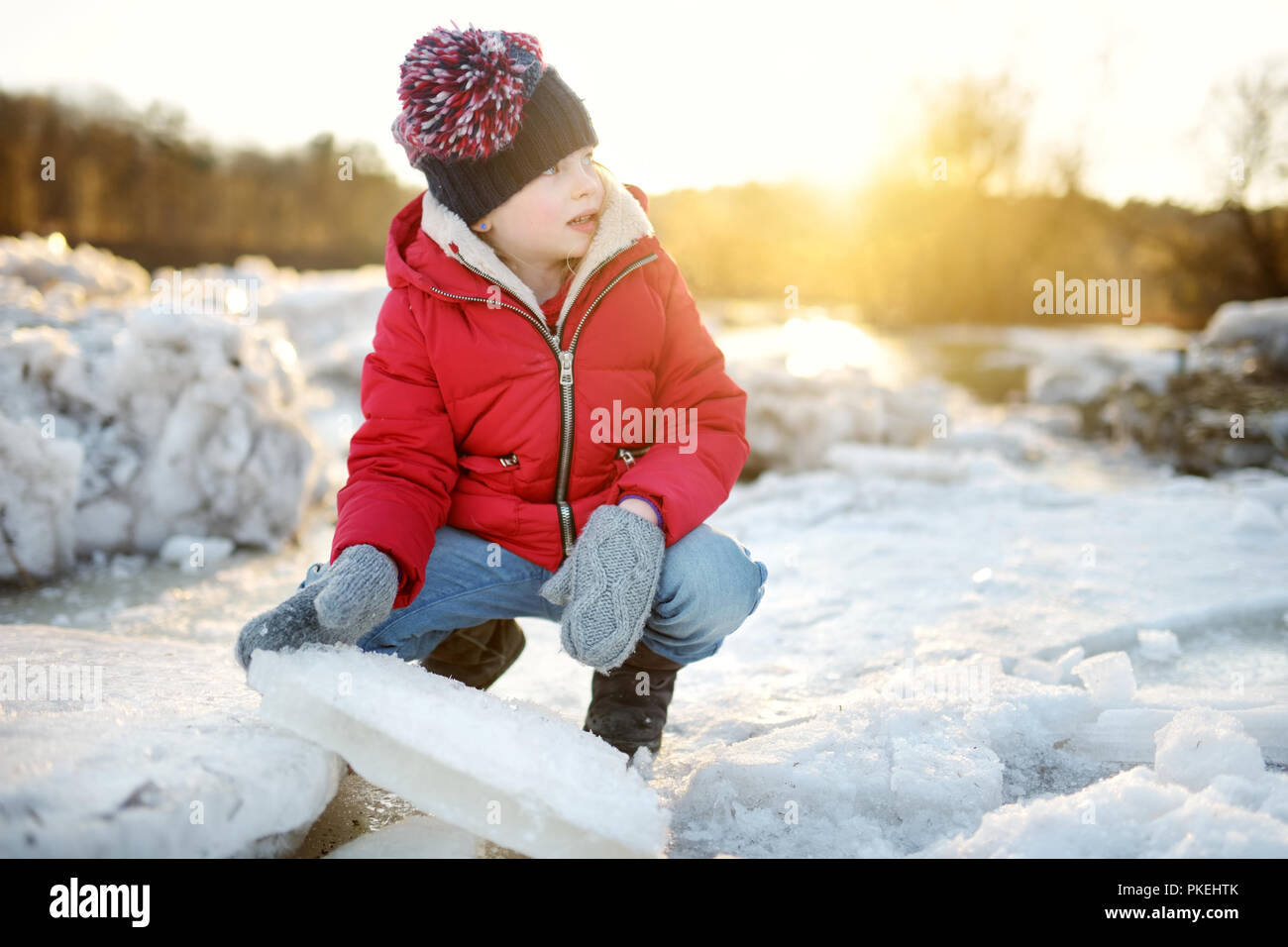 Happy little girl playing with ice blocks by frozen river during an ice ...