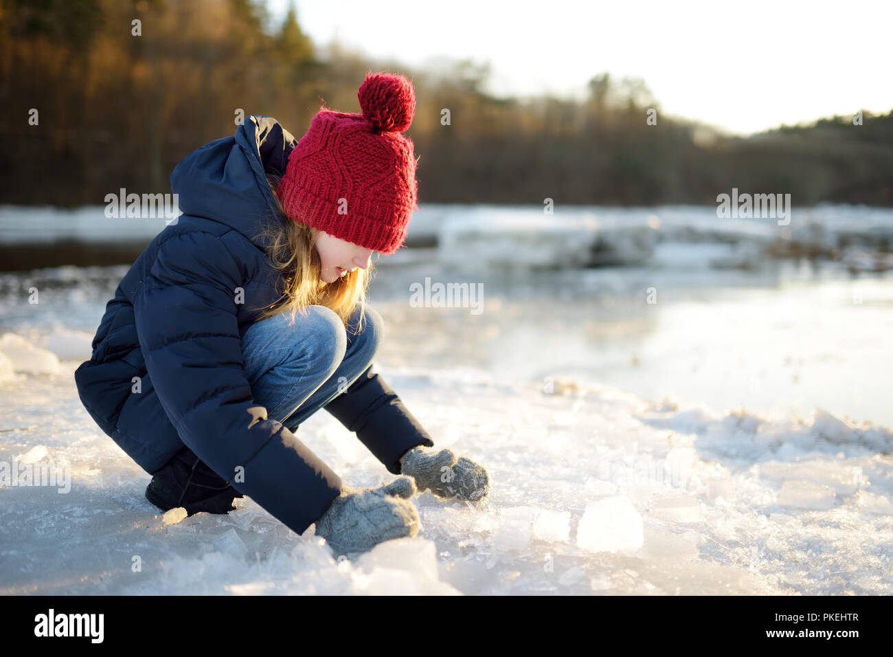 Happy little girl playing with ice blocks by frozen river during an ice ...