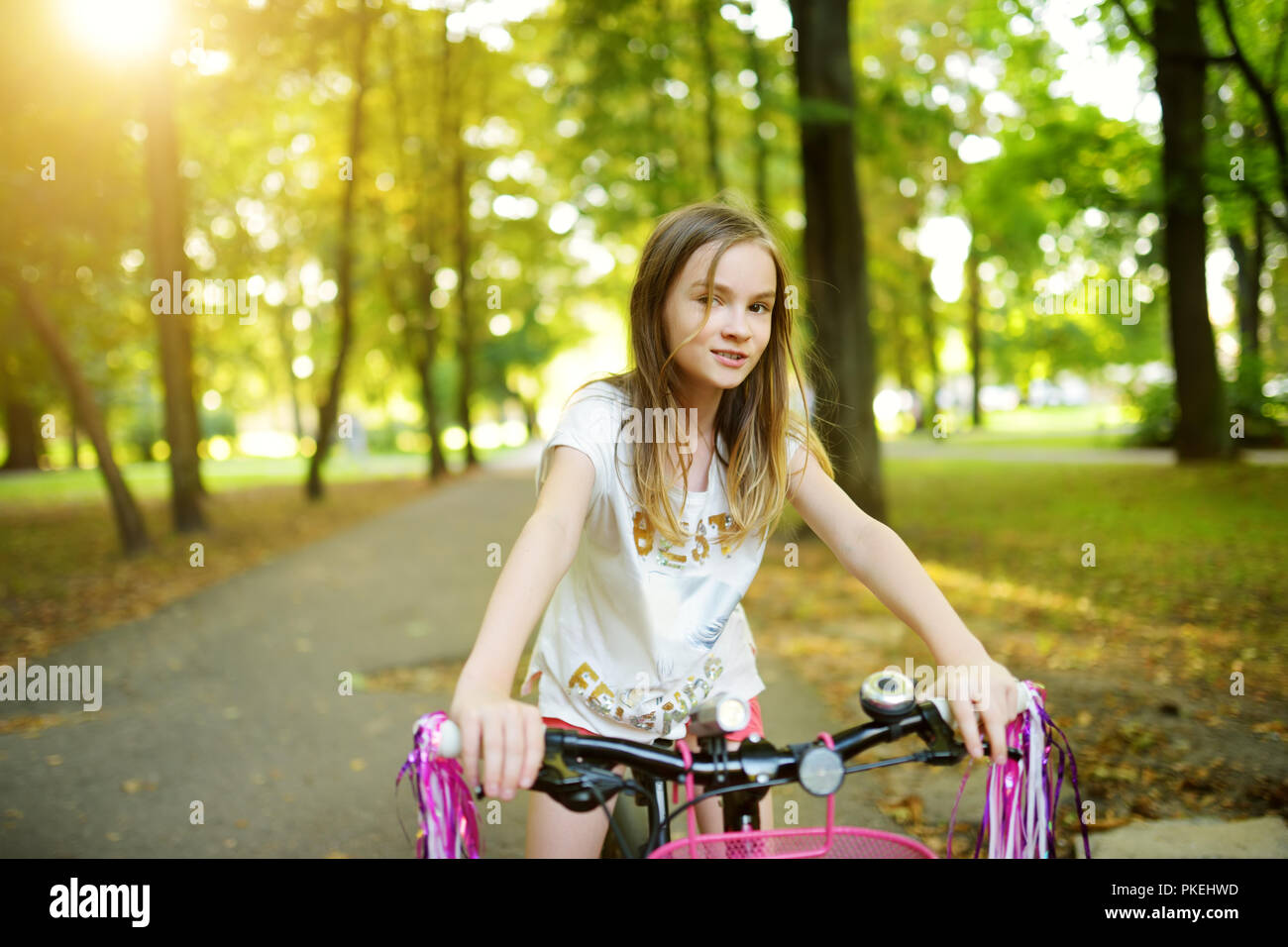 Cute little girl riding a bike in a city park on sunny summer day ...