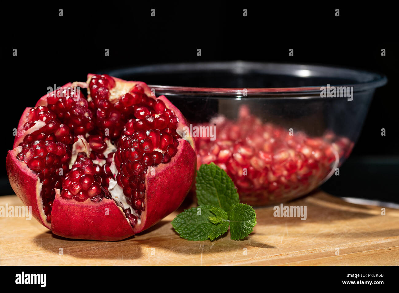 Open pomegranate layed next to a mint leaf and bawl of seeds displayed ...