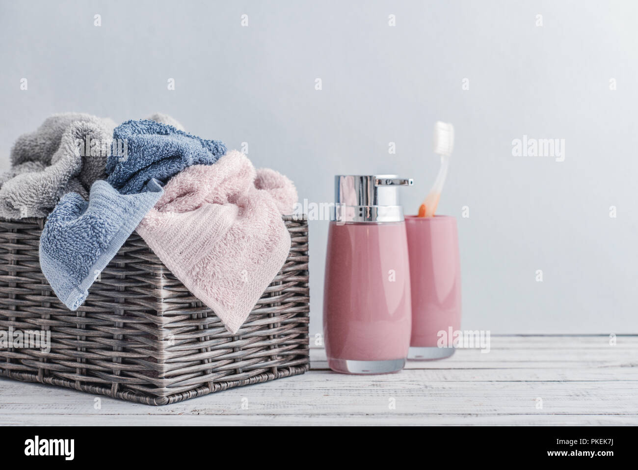 Dispenser, teeth brush and towels in a wicker basket on a light ...