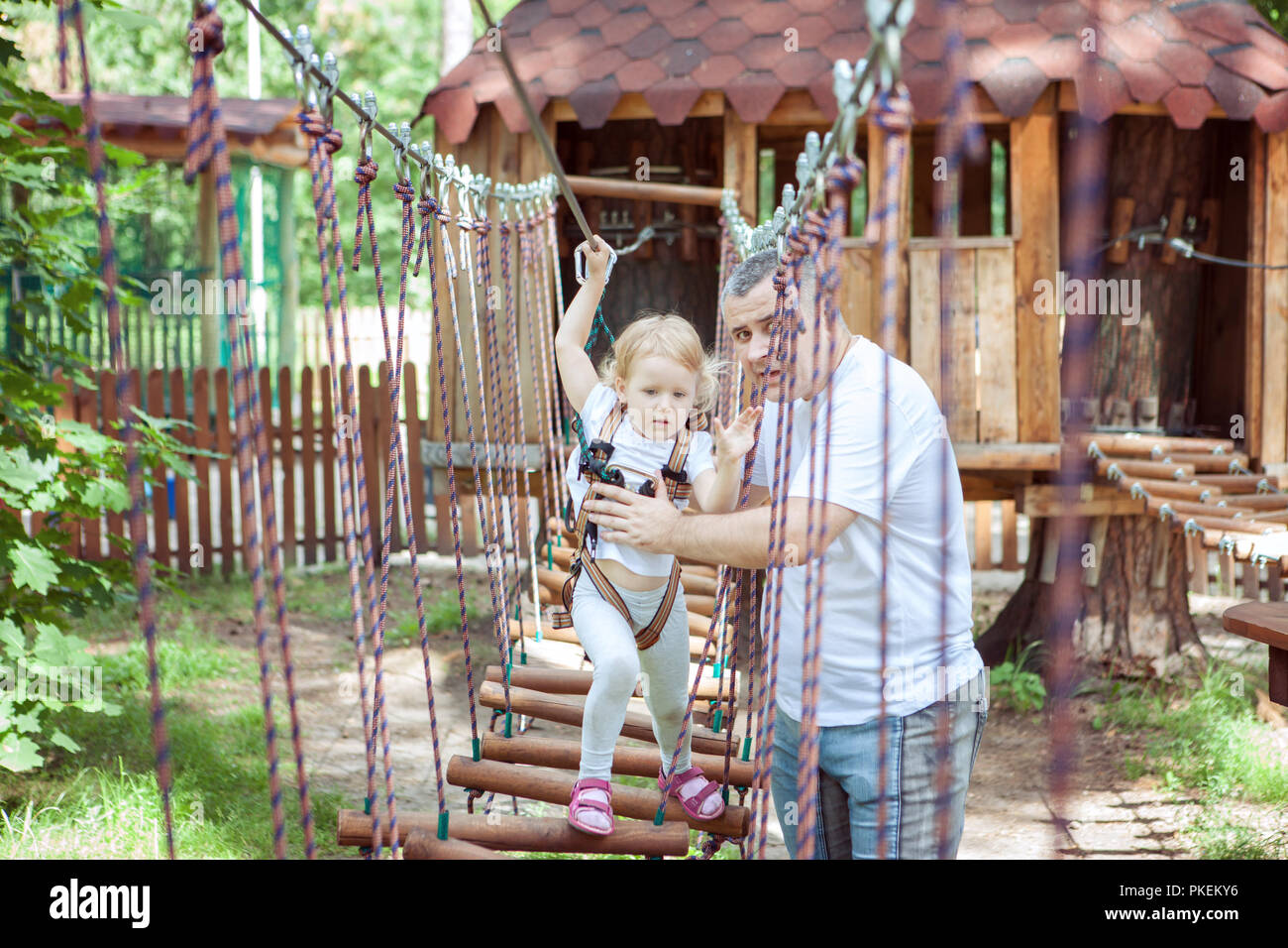 Young father helping his little daughter on the obstacle in the rope ...