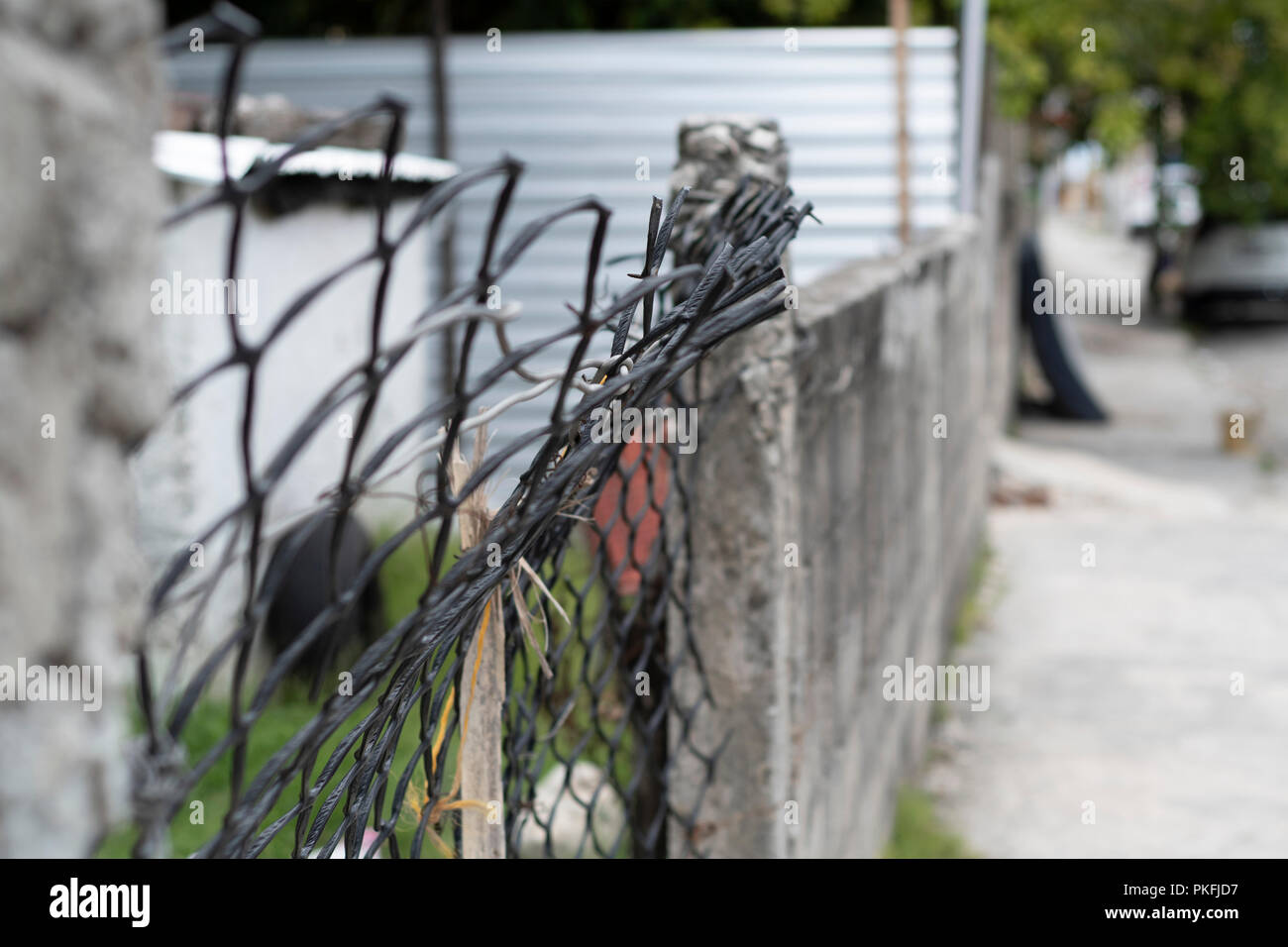 Broken wire fence with blurred concrete fence and street in the ...
