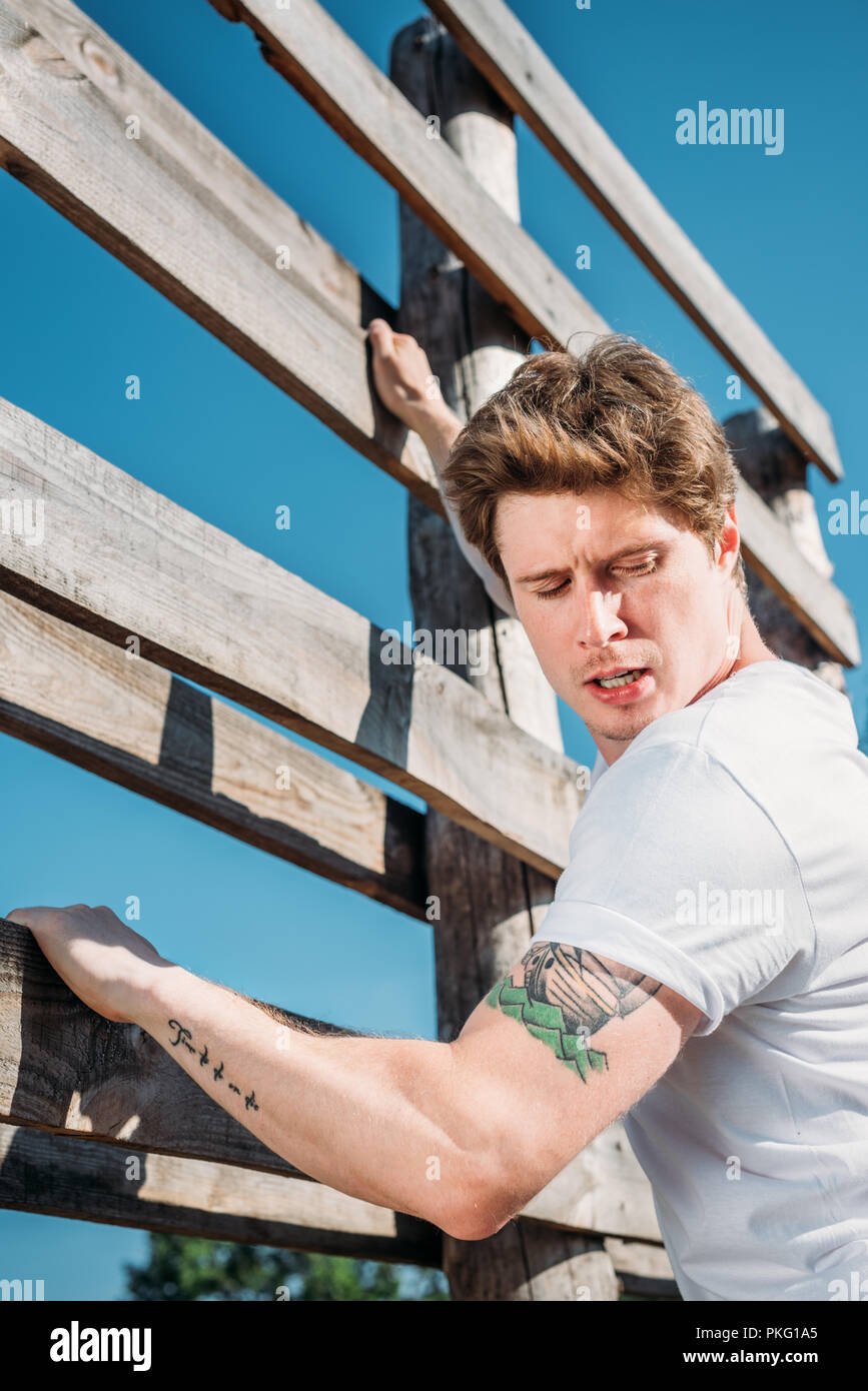 side view of young soldier climbing wooden barrier during obstacle run ...
